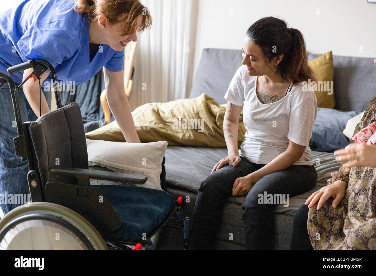 Nurse setting wheelchair for woman with paraplegia sitting on sofa at ...