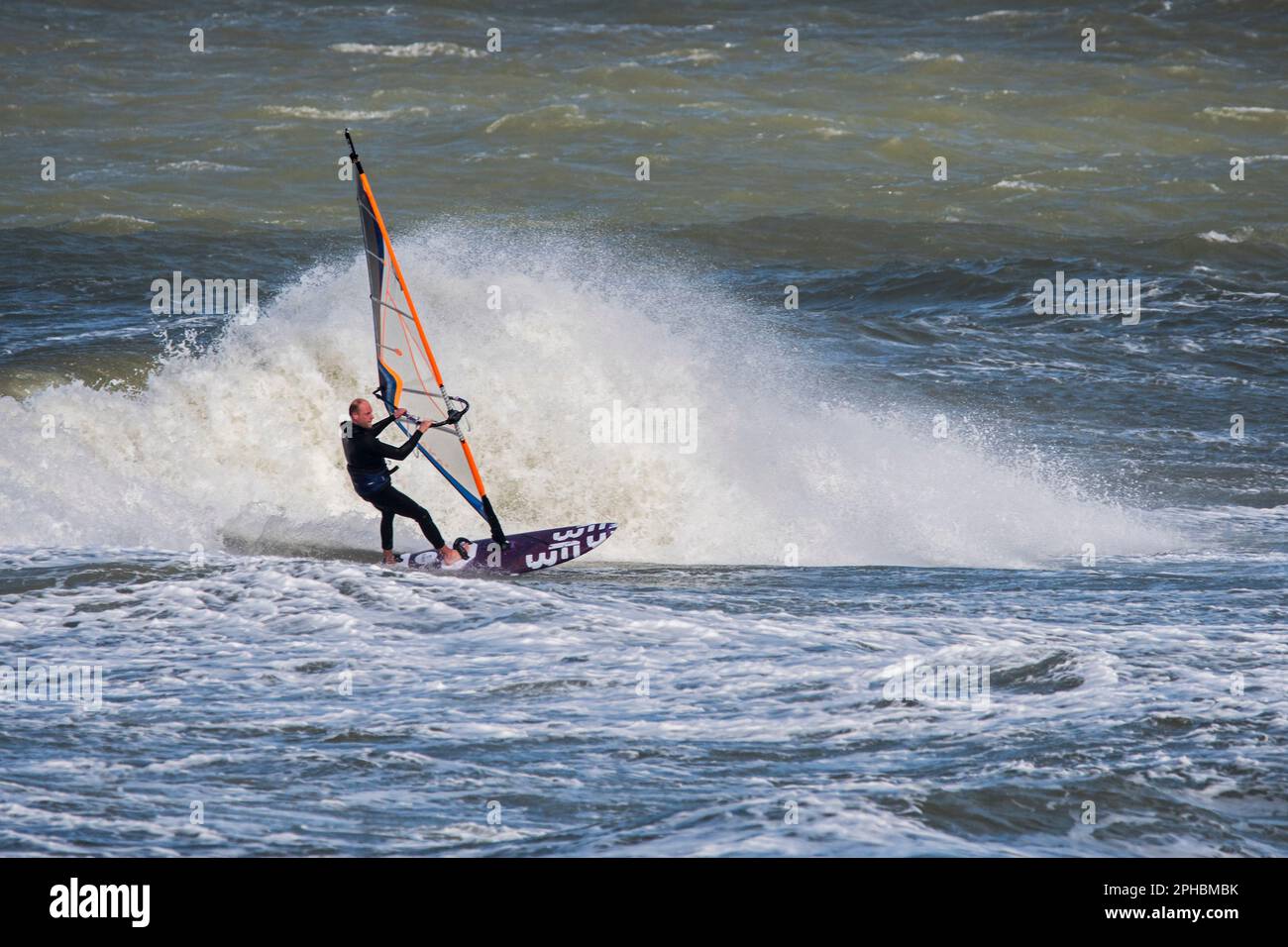 Recreational windsurfer in black wetsuit practising classic windsurfing ...
