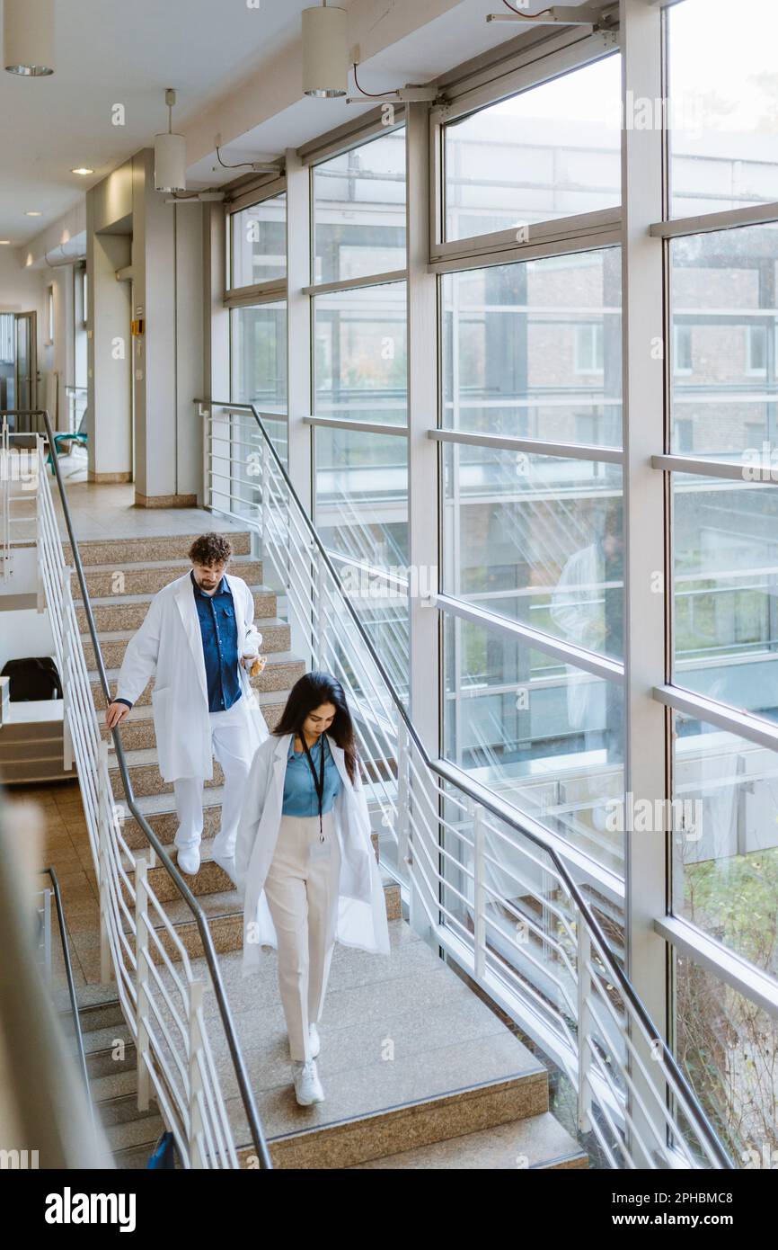 Full length shot of male and female physicians moving down on staircase ...