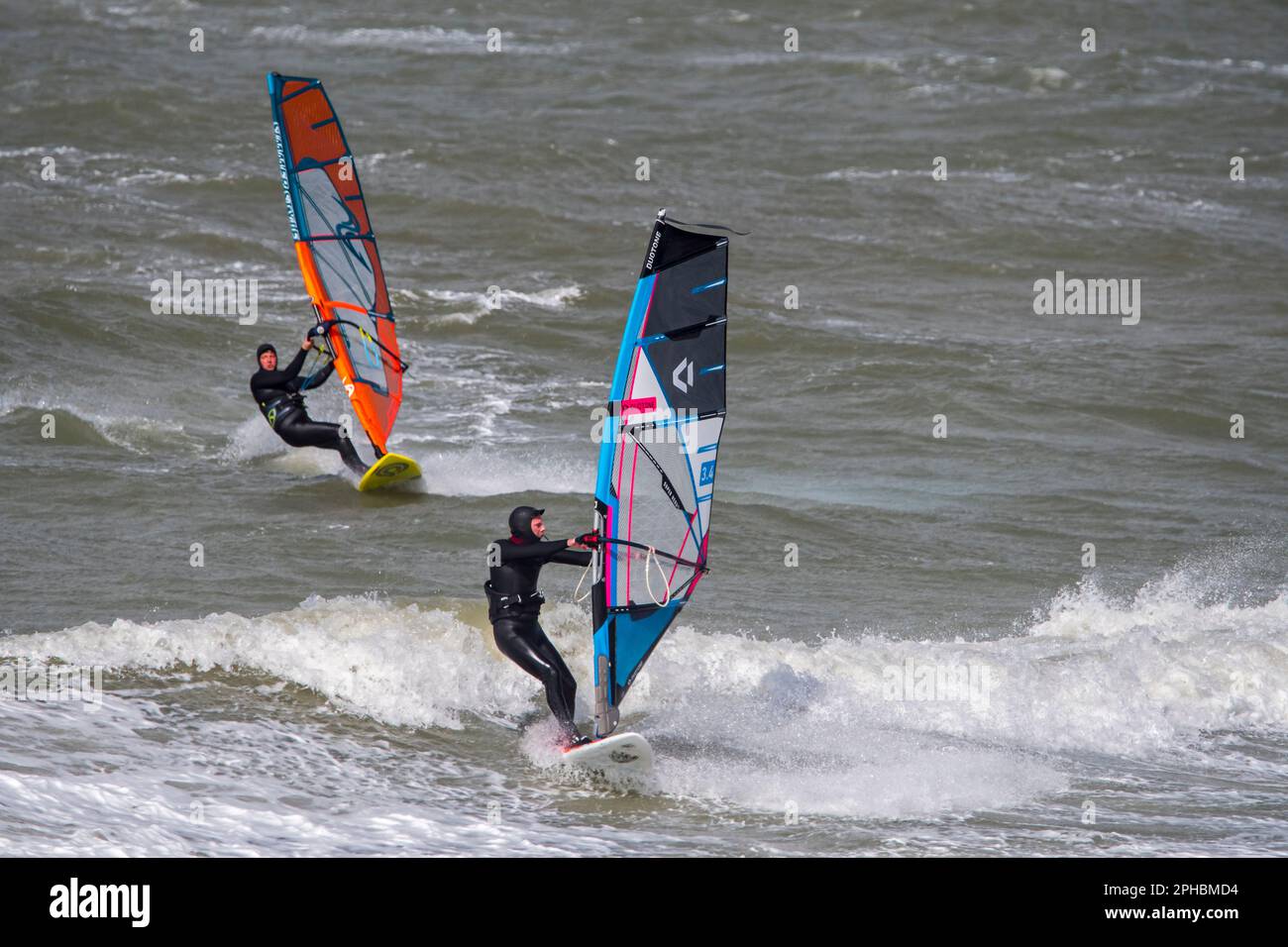 Two recreational windsurfers in black wetsuits practising classic ...