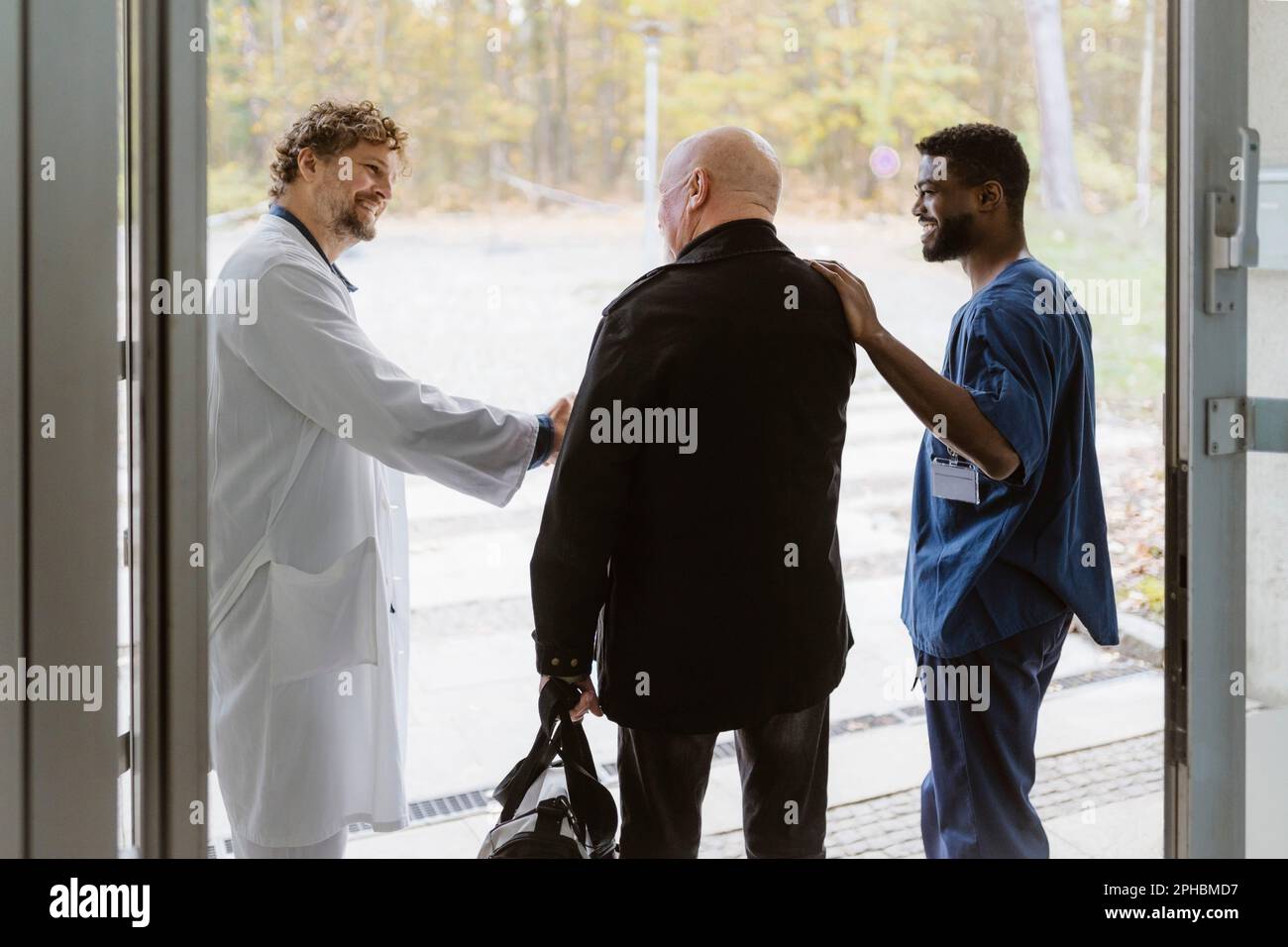 Senior male patient shaking hands with doctor while standing by nurse ...