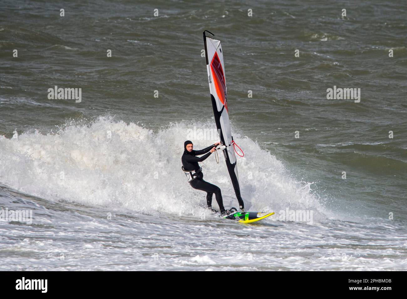 Recreational windsurfer in black wetsuit practising classic windsurfing ...