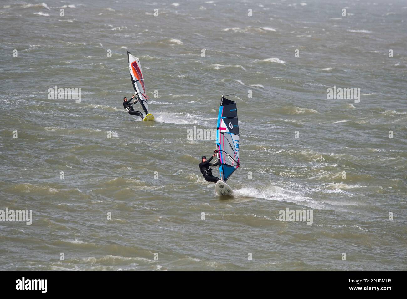 Two recreational windsurfers in black wetsuits practising classic ...