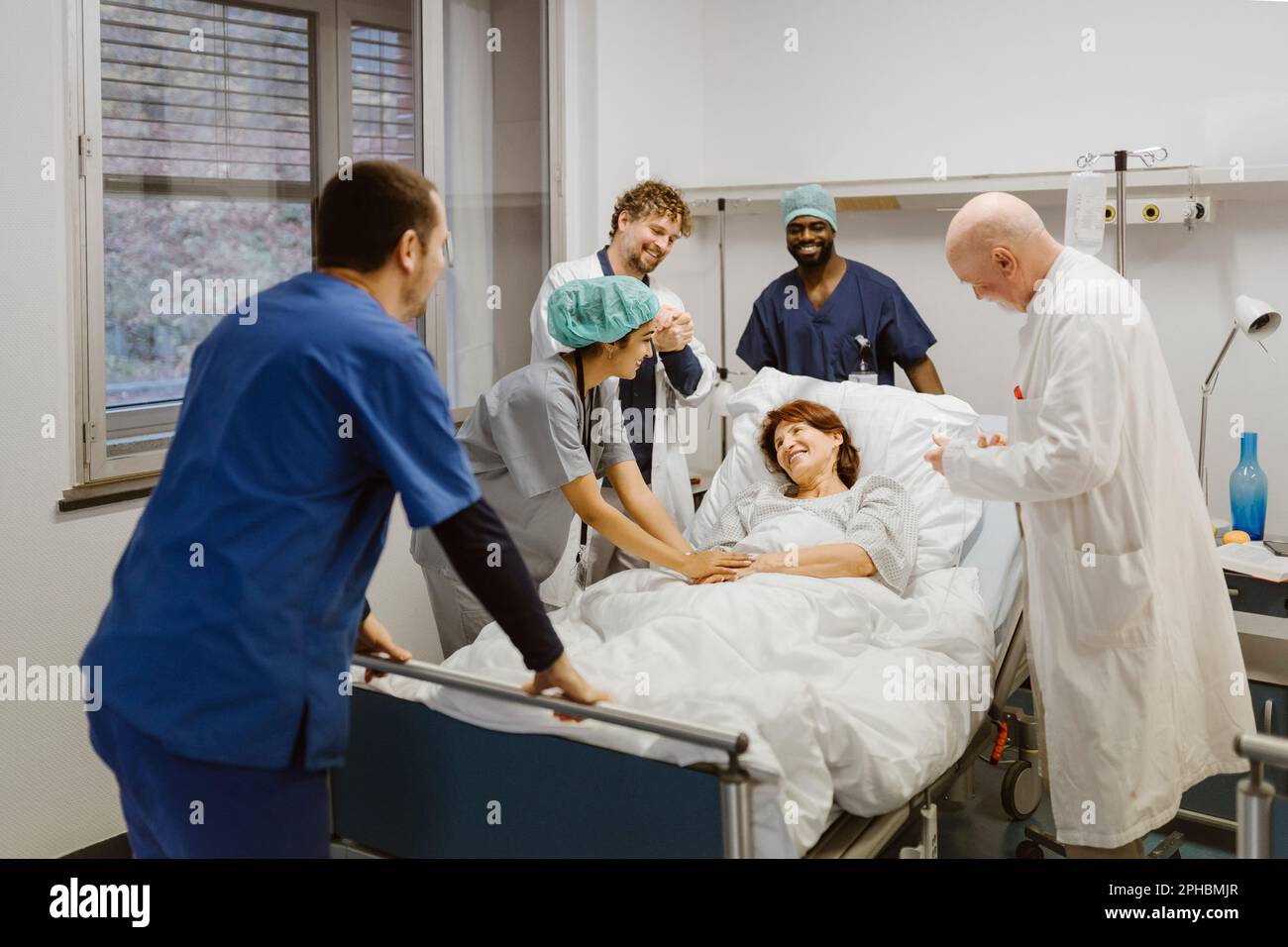 Smiling healthcare workers cheering while standing around senior female ...