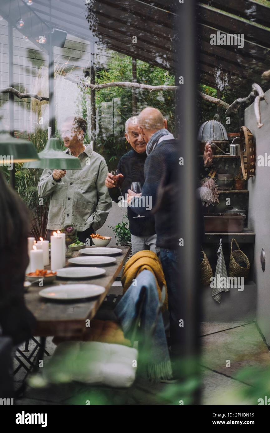 Male friends talking to each other at dinner party seen through glass ...