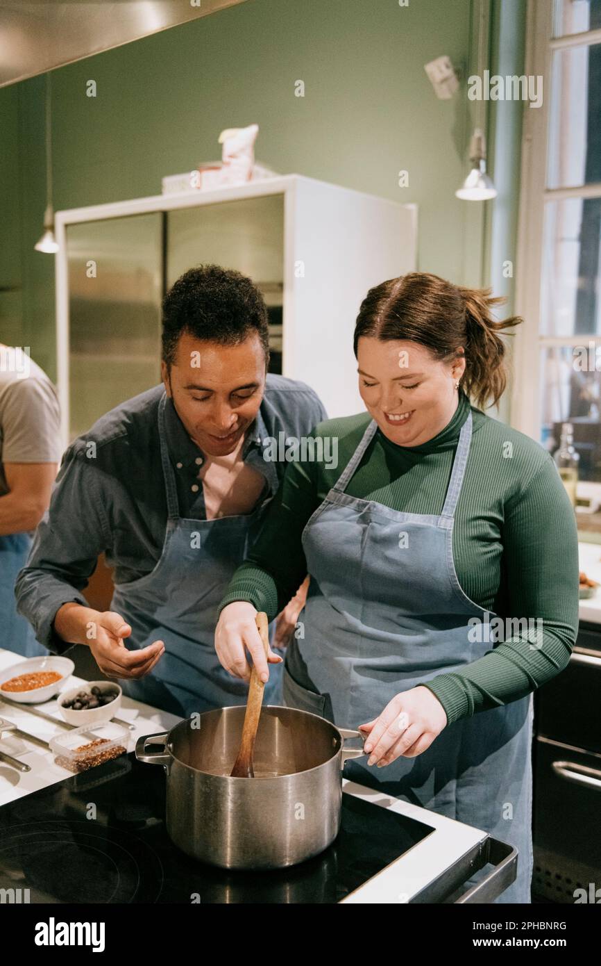Male and female students preparing food during cooking class in kitchen ...