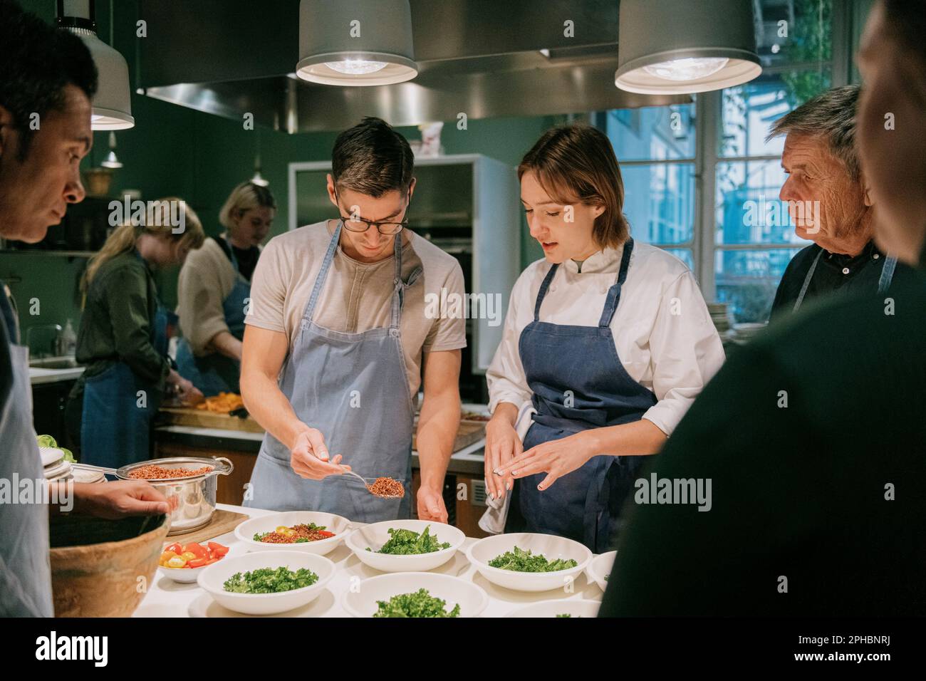 Female chef assisting male student during cooking class in kitchen ...