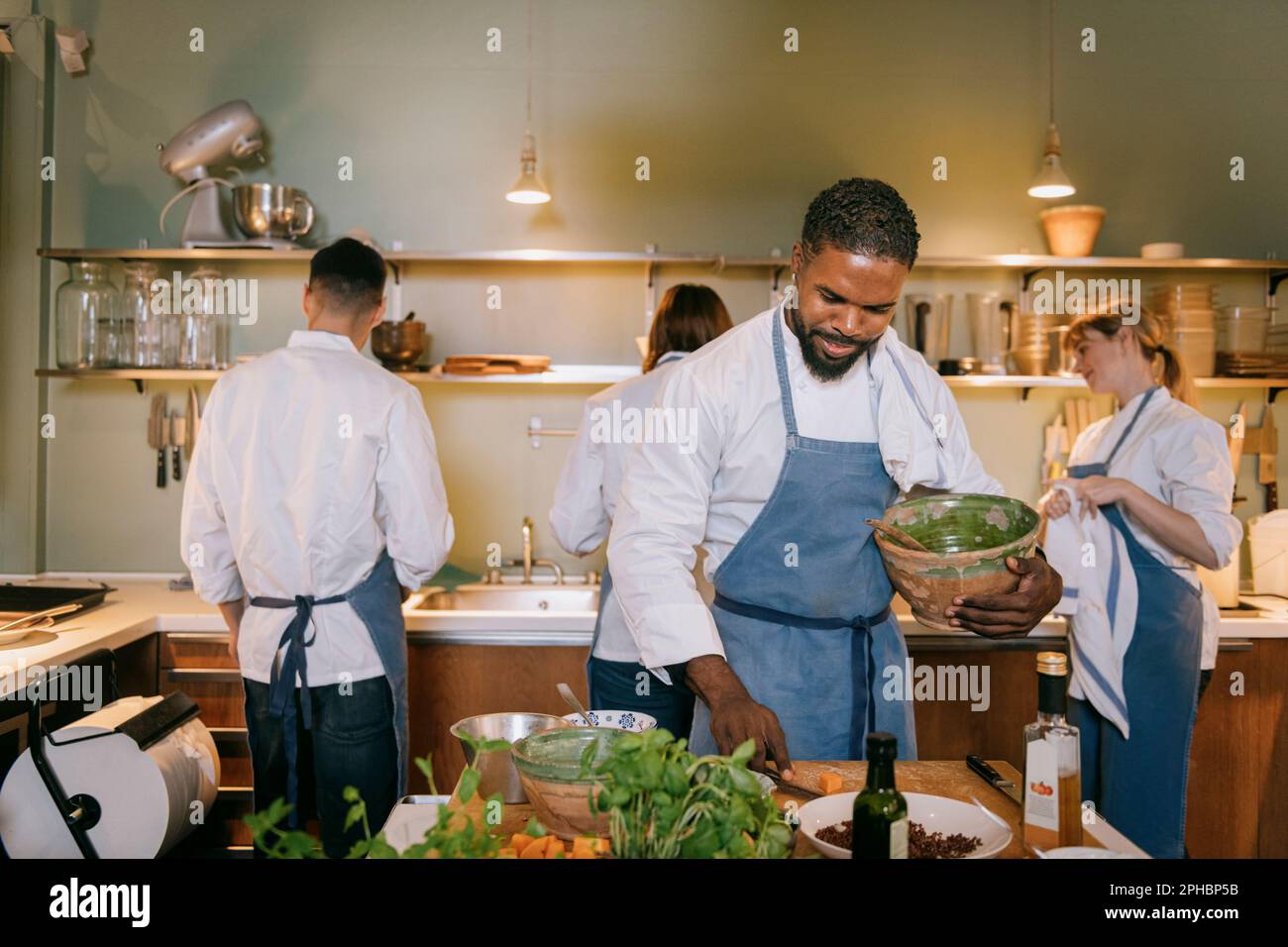 Male chef holding bowl while preparing food in commercial kitchen Stock ...