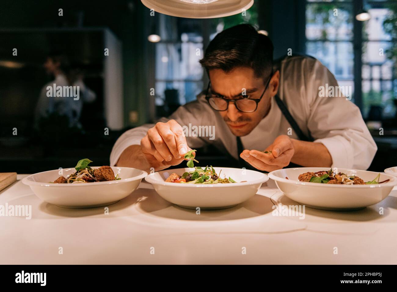Male chef plating food in plate while working in commercial kitchen ...