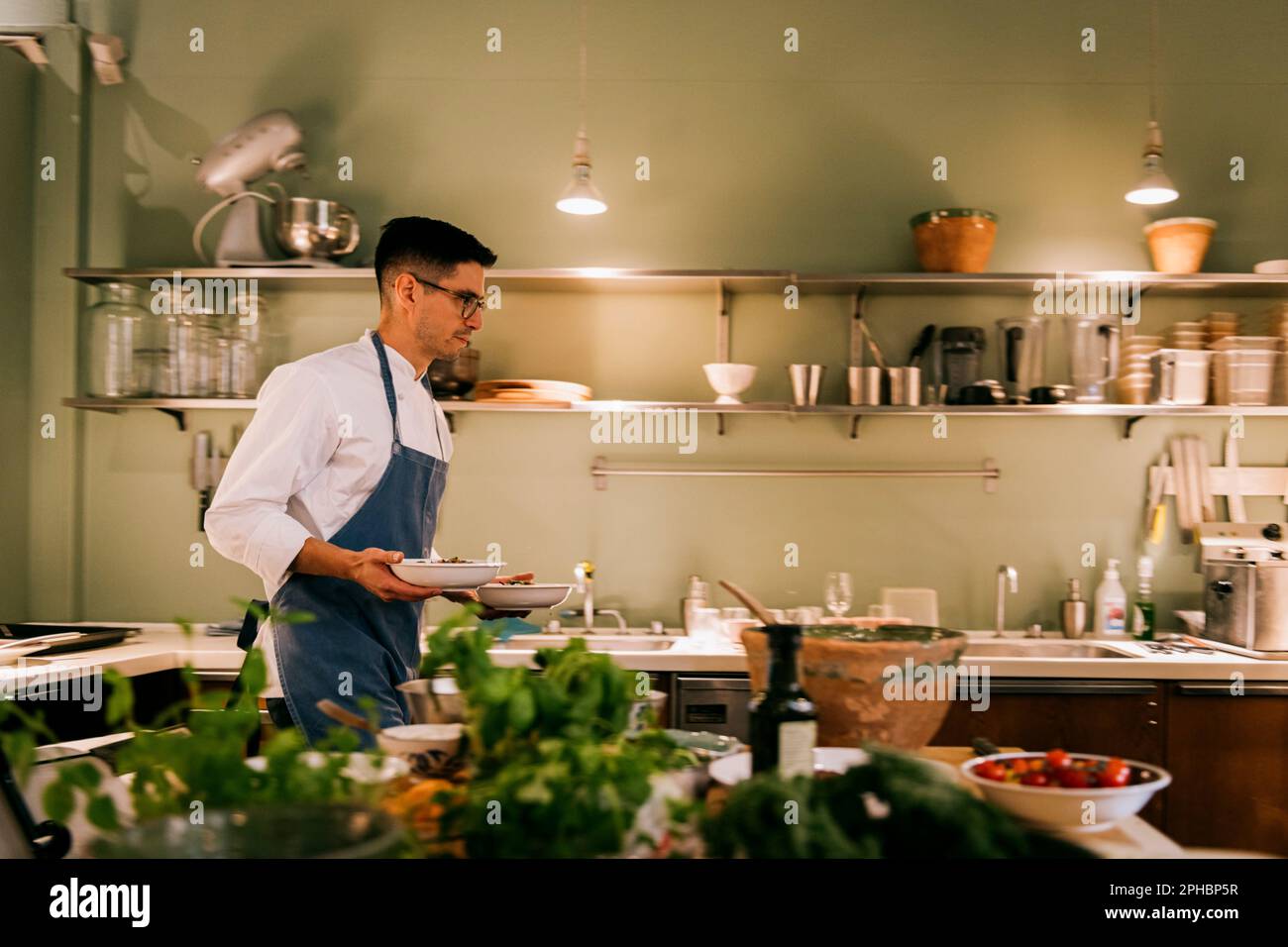 Male chef holding plates while working in commercial kitchen Stock ...