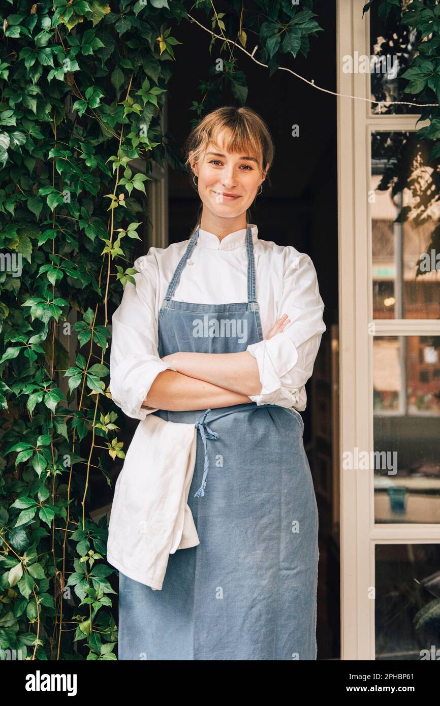 Portrait of smiling female chef standing with arms crossed outside ...