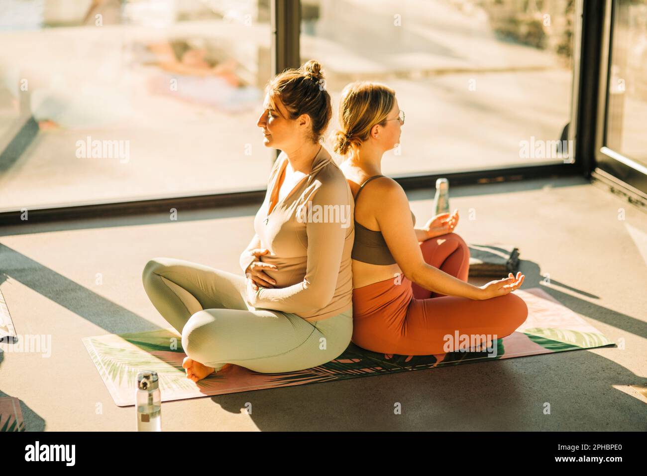 Women practicing breathing exercise sitting back to back during yoga ...
