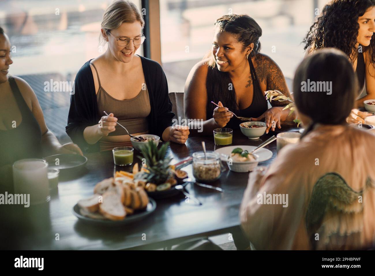 Female friends talking to each other while having breakfast at retreat ...