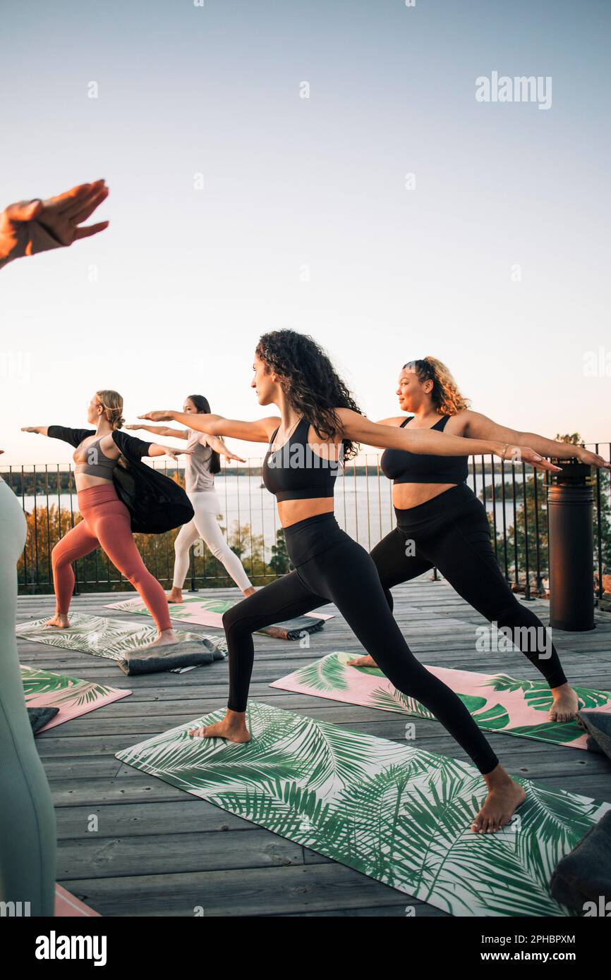 Female friends practicing Warrior 2 pose on patio at sunset Stock Photo ...