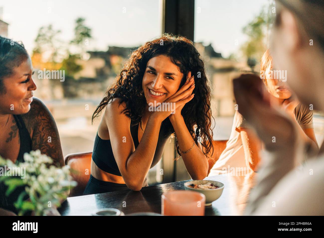 Happy woman leaning on elbows while talking to female friends at ...