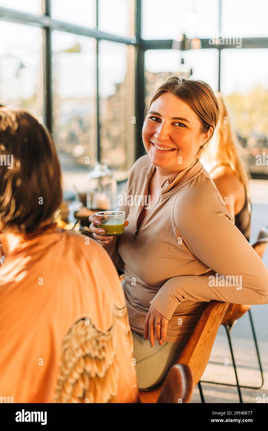 Portrait of smiling woman sitting on chair while having breakfast at ...
