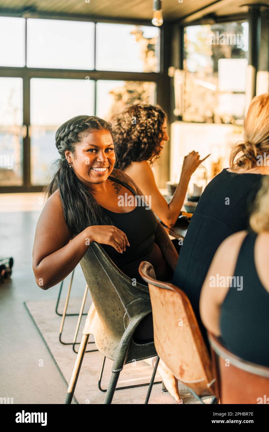 Portrait of smiling woman with female friends sitting on chair at ...