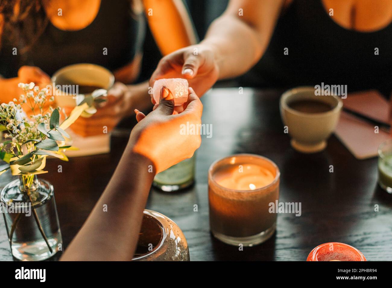 Hand of woman passing crystal to female friend over burning candle at ...