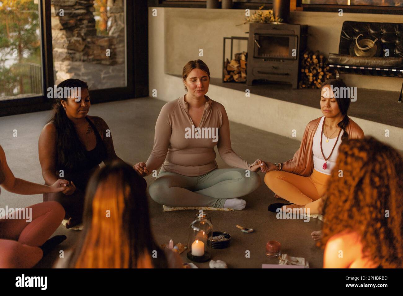 Multiracial female friends holding hands while doing meditation at ...