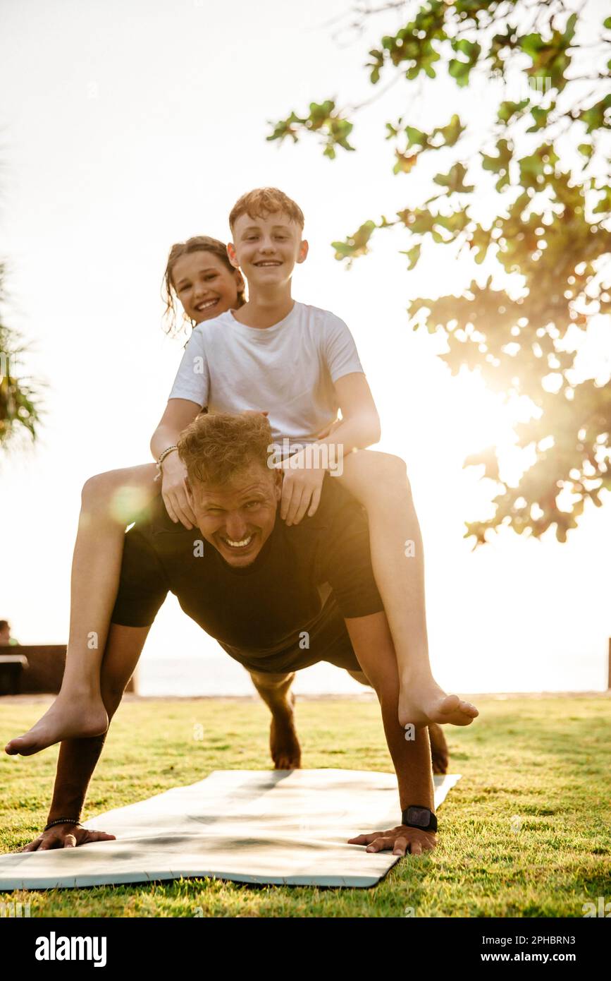Father carrying children on back while practicing push-ups in park ...