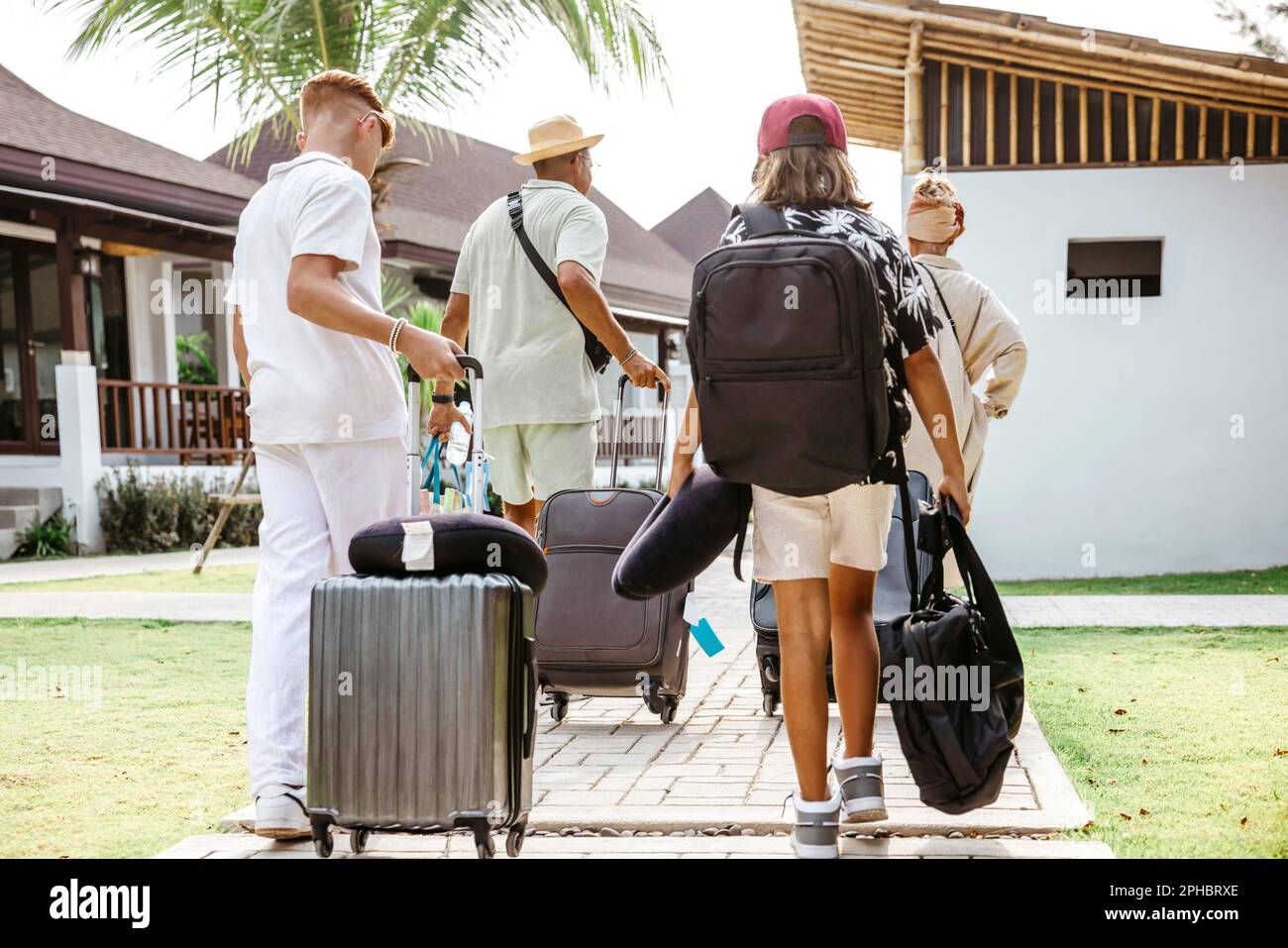 Rear view of family walking with wheeled luggage at resort during ...