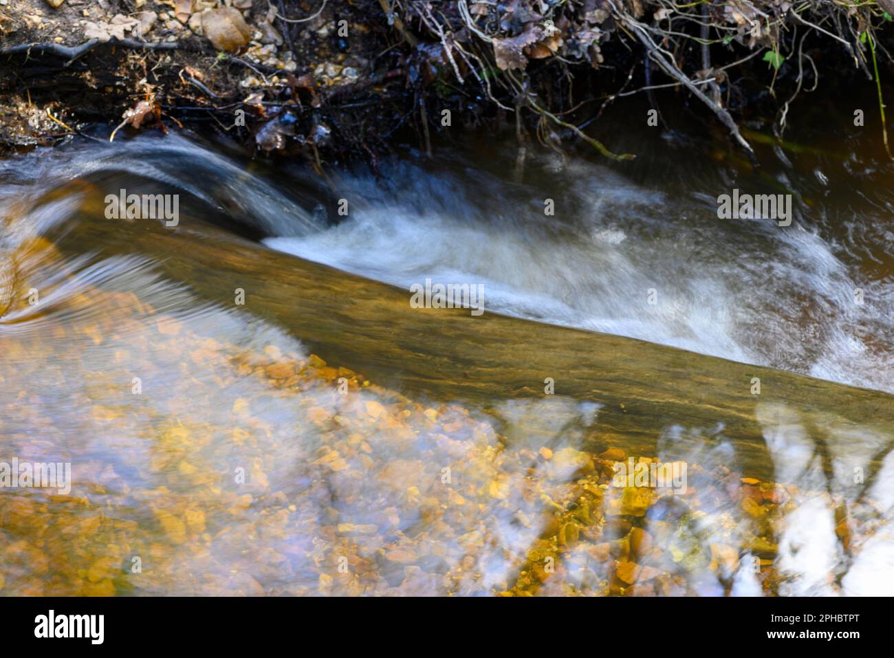 Fast flowing water in a stream running over a log, blurred motion Stock ...