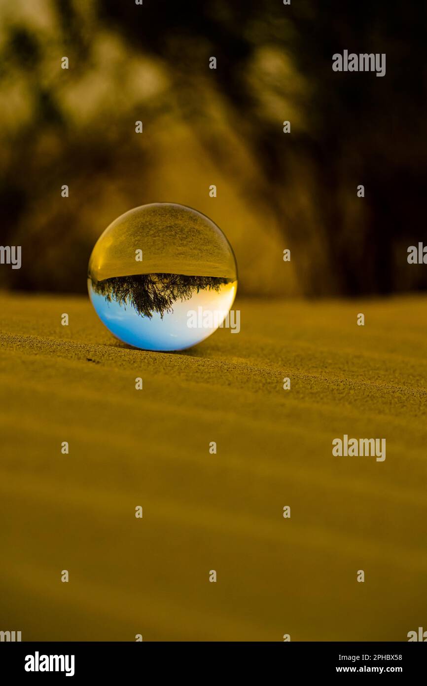 A glass ball resting on sands in a natural environment, with blurred ...
