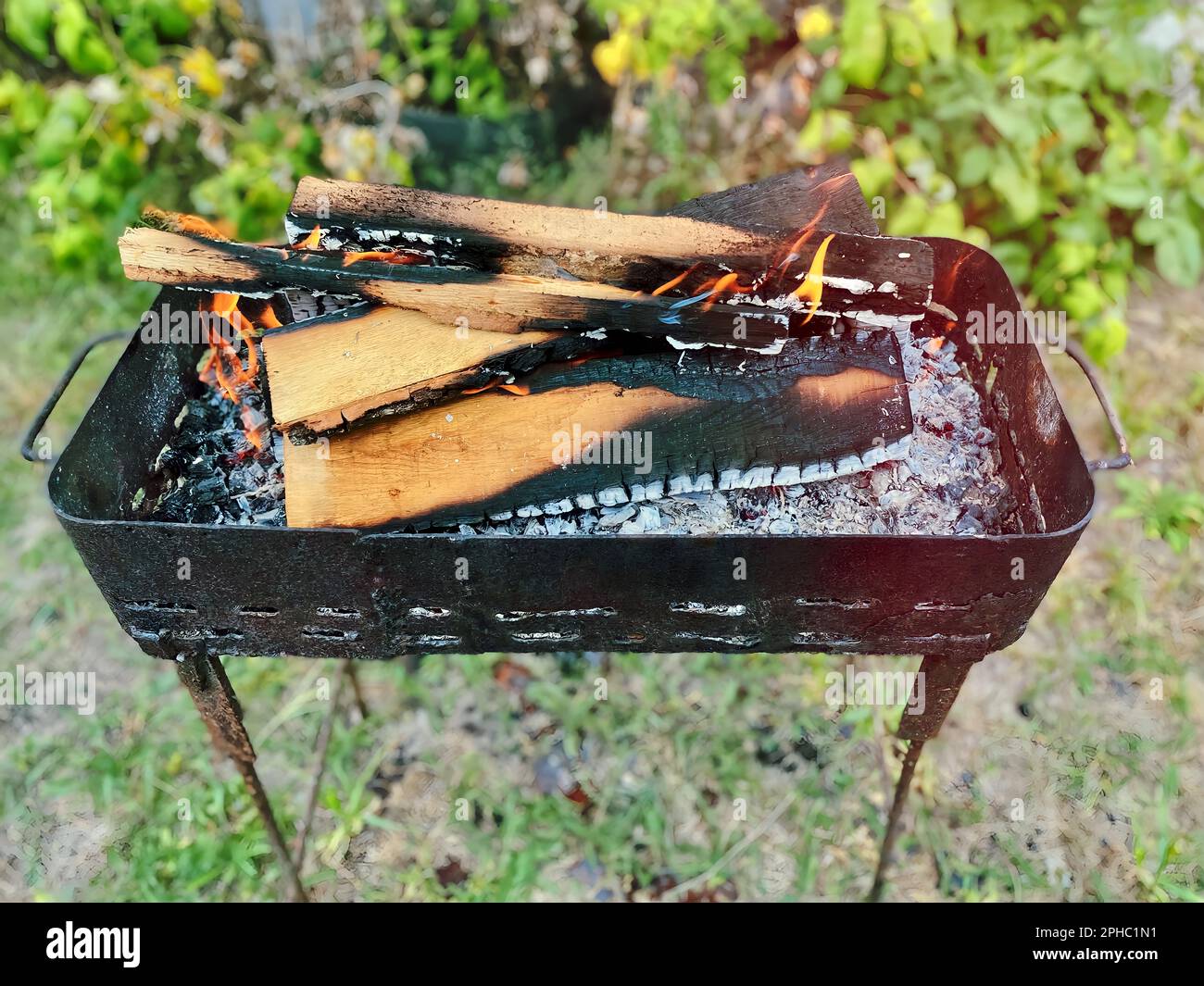 Burning wood in the grill. Small folding portable brazier filled with ...
