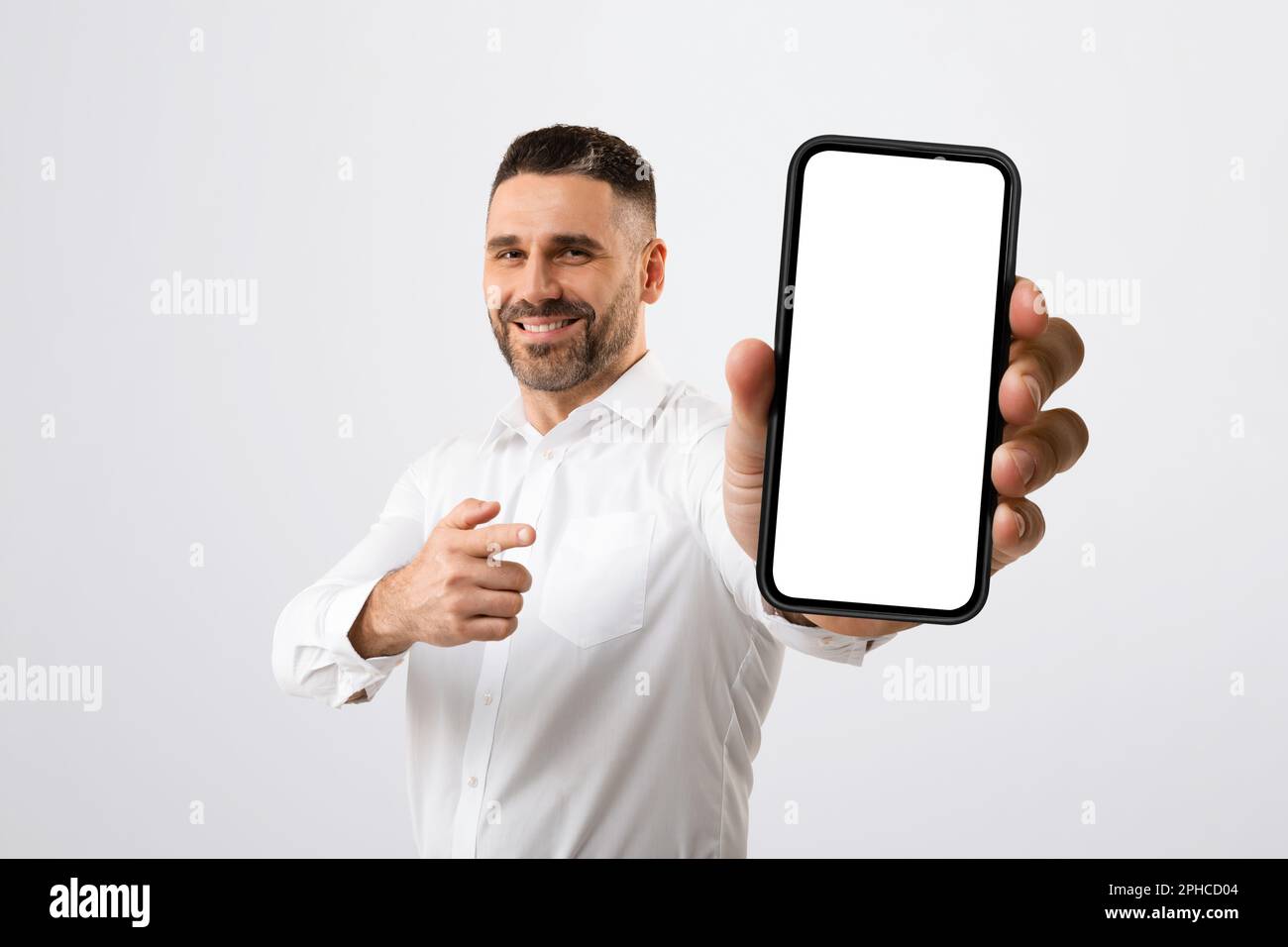 Positive male entrepreneur pointing at giant blank smartphone screen ...