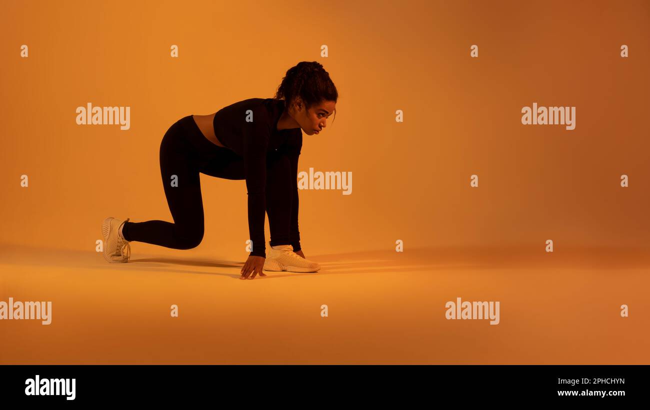 Fit black sportswoman doing crouch start ready for running on neon ...