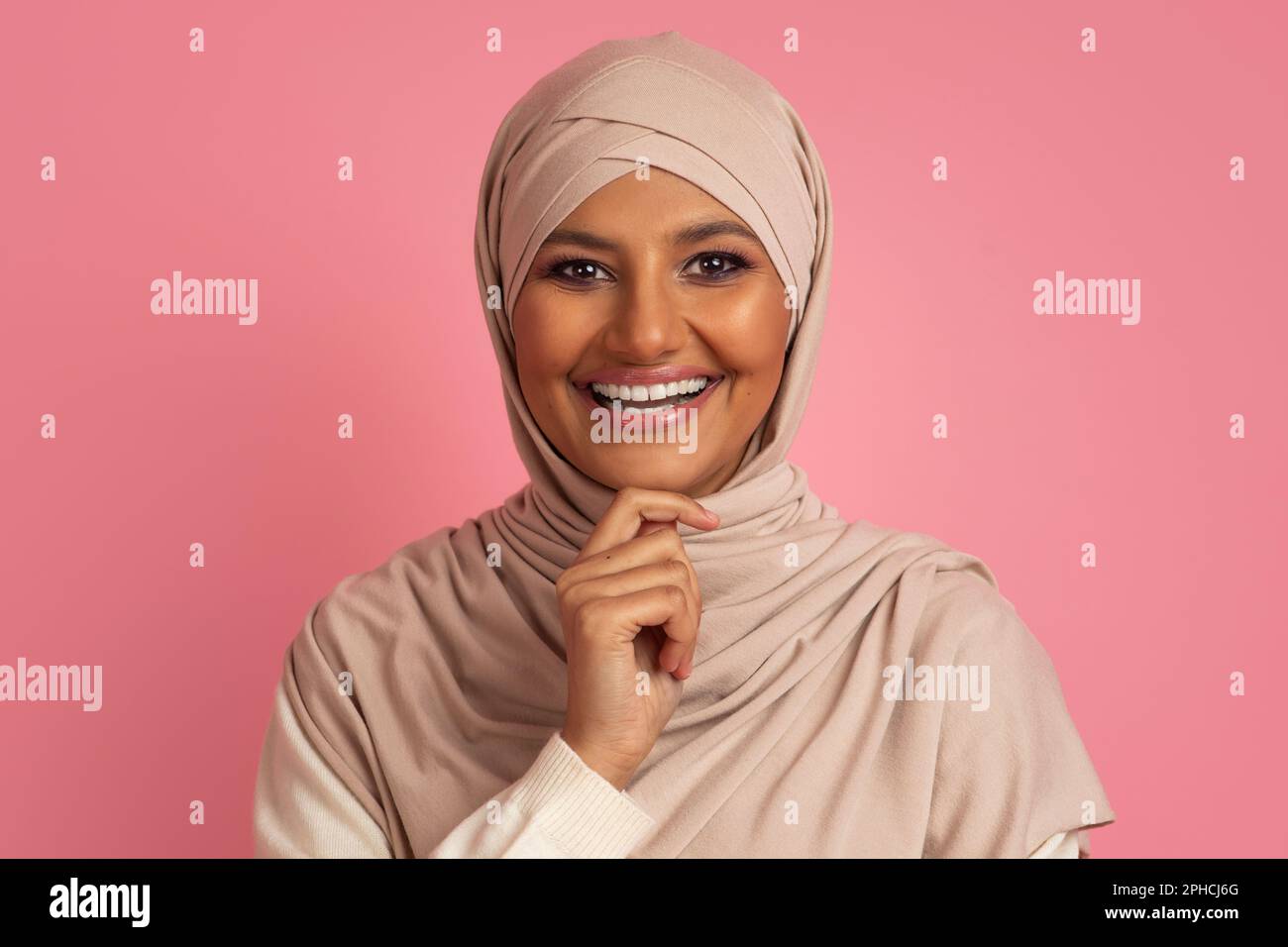 Beautiful muslim woman in hijab touching her chin and smiling at camera ...