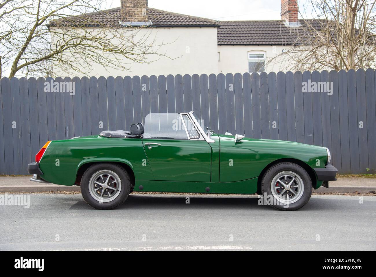 Green MG Midget parked by a grey wooden fence with a house behind on a ...