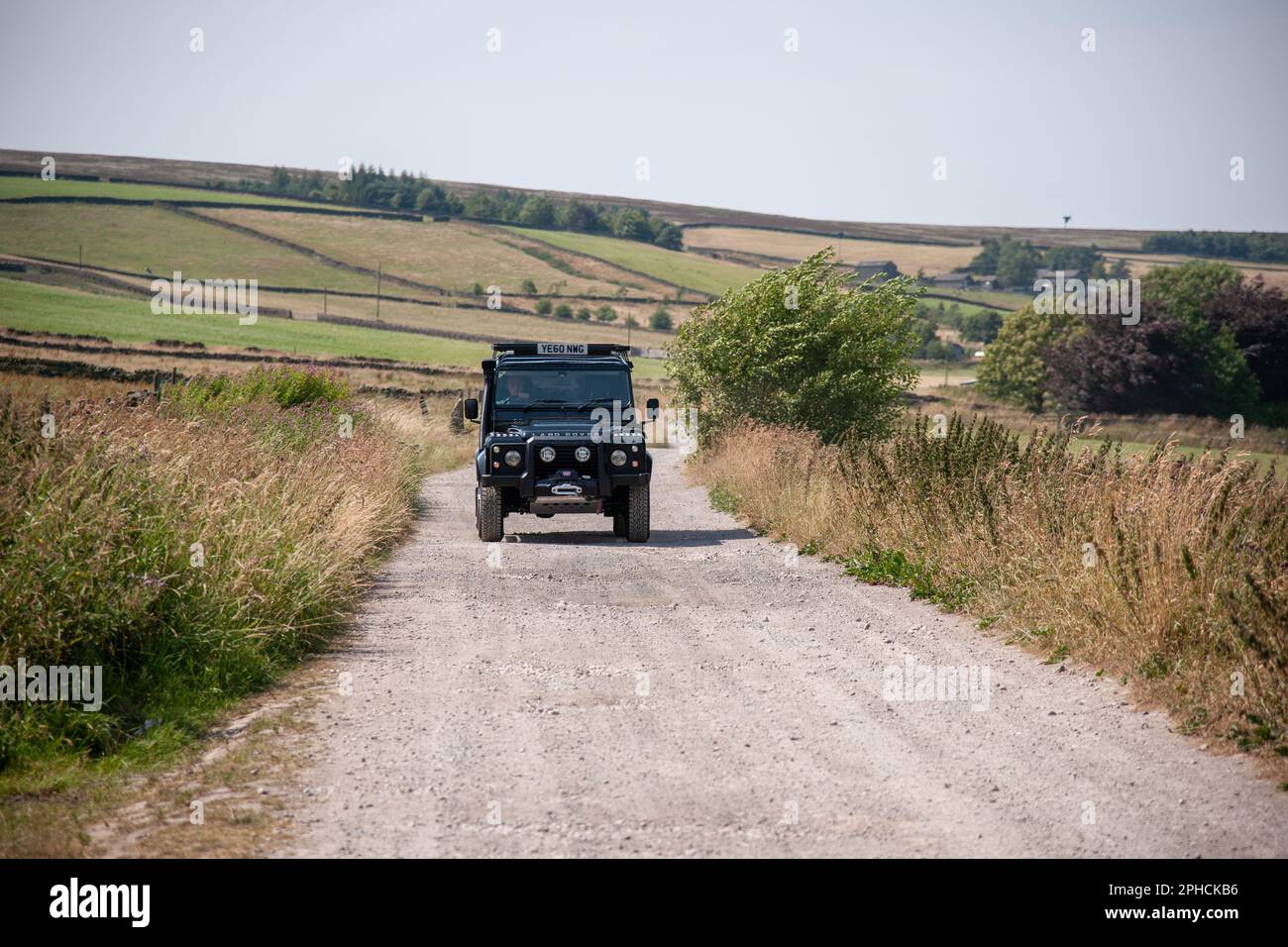 Black Land Rover Defender 110 long wheelbase driving down a gravel farm ...