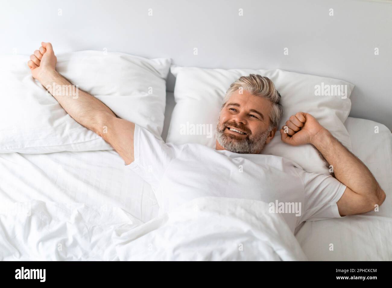 Happy middle aged man stretching in bed in the morning Stock Photo - Alamy