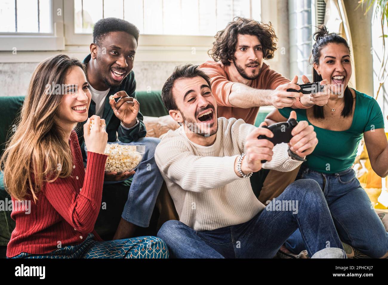 Happy multi ethnic friends sitting on sofa playing video games ...