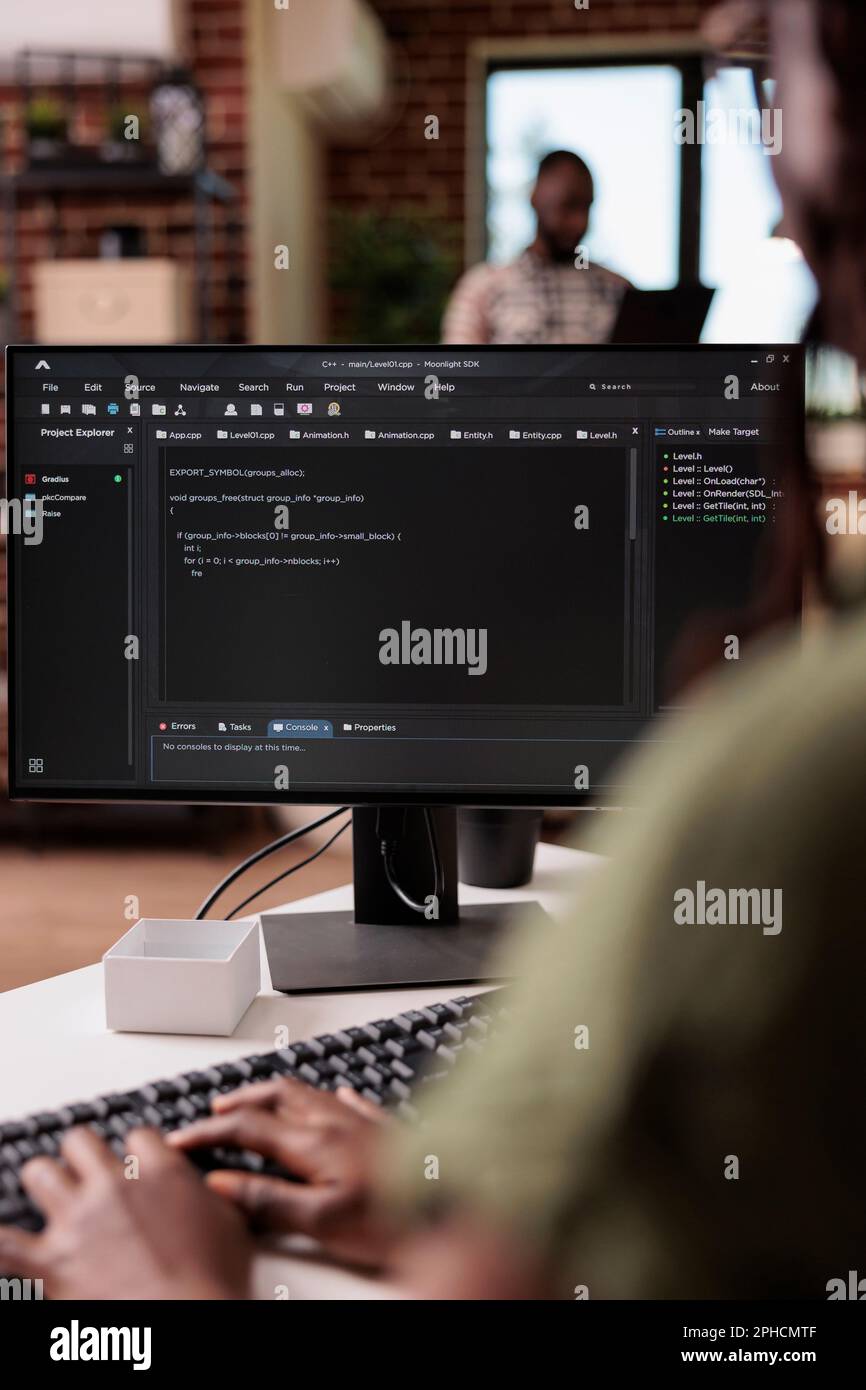 Selective focus on programmer typing code on computer keyboard while roommate is relaxing using ...