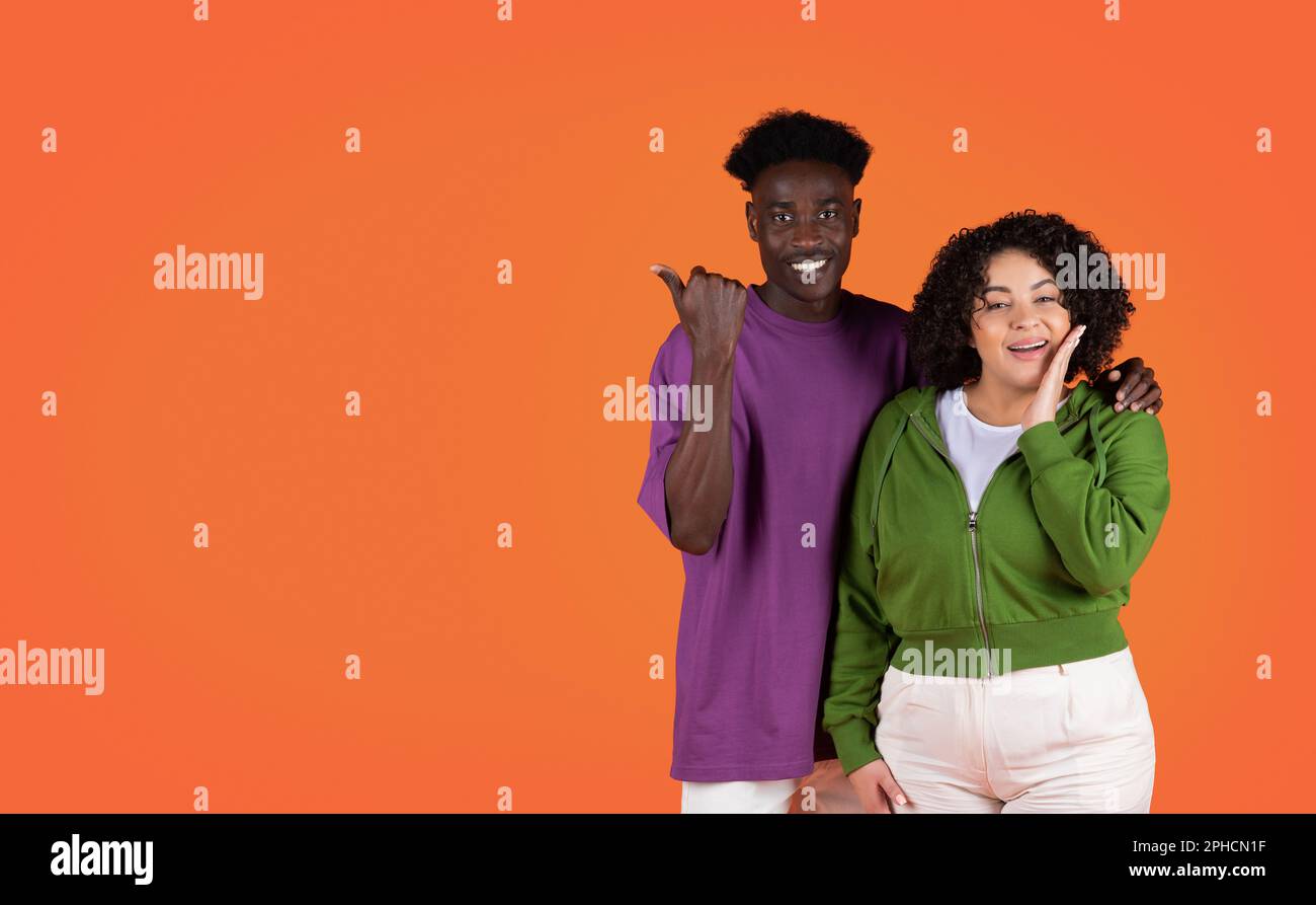 Cute multicultural couple embracing and showing free space on red Stock ...
