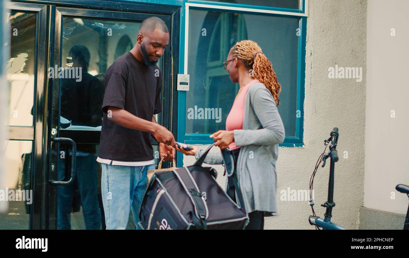 Female delivery person giving food package to client, man paying for ...