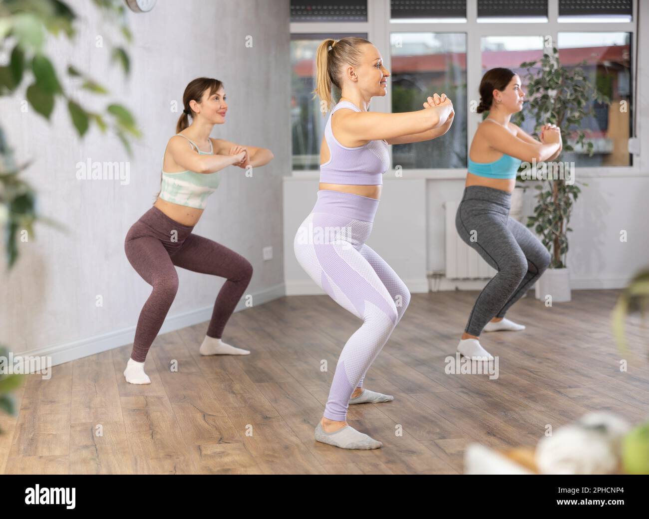 Inspired young fit women in tight sports clothes doing squats during ...