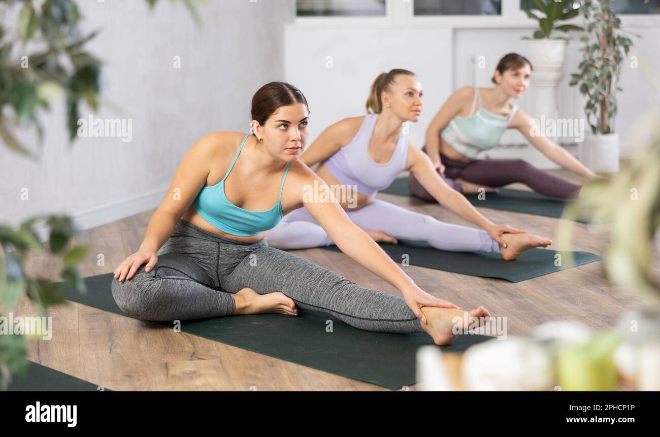 Diligent women practicing hand to toe pose of yoga in light fitness ...