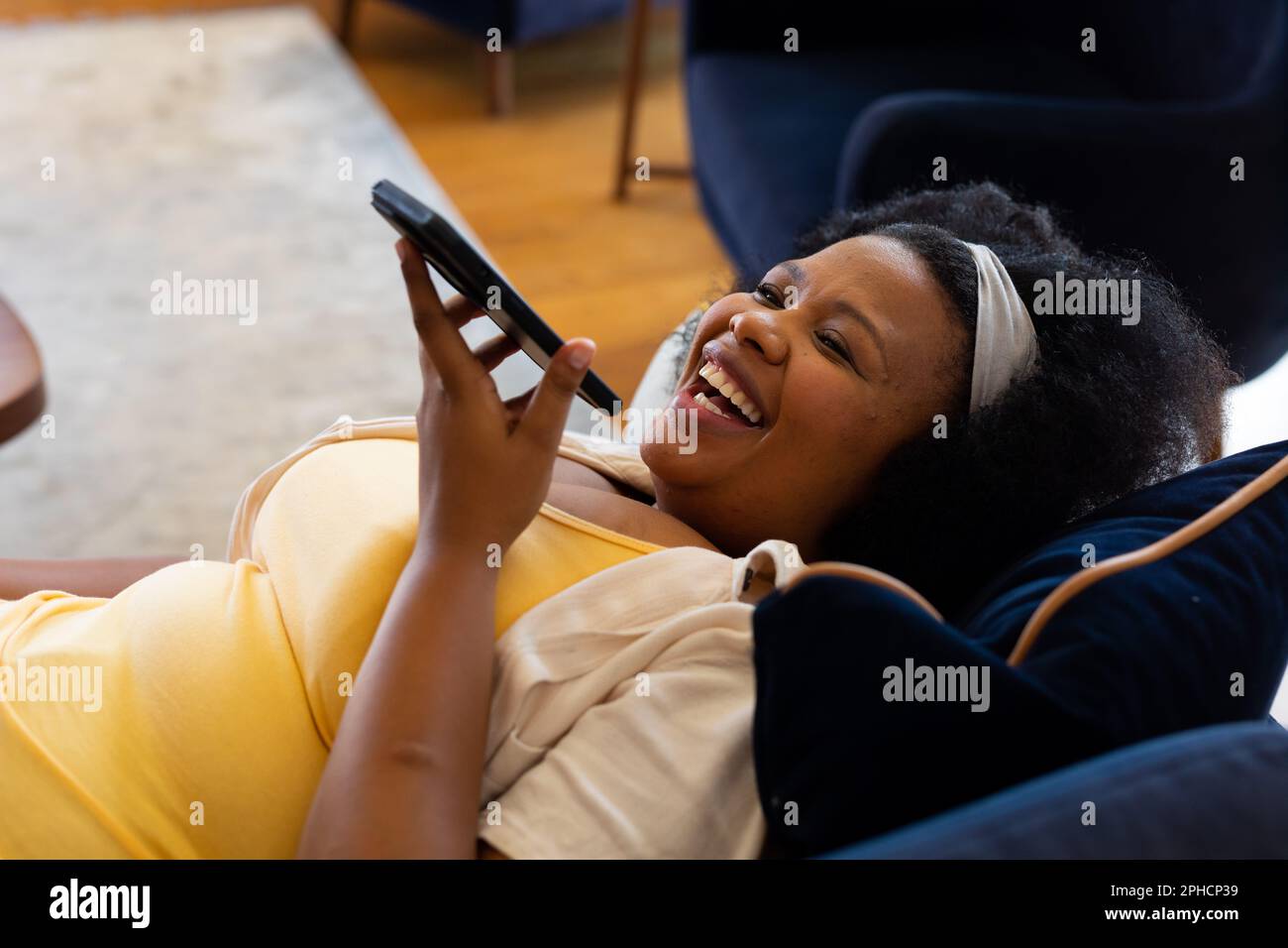 Happy plus size african american woman lying on sofa, talking on ...
