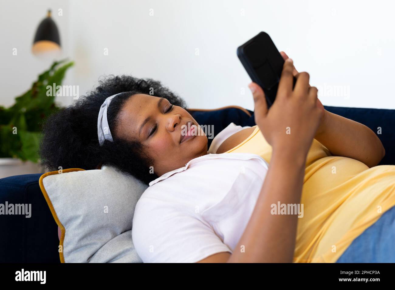 Happy plus size african american woman lying on sofa and using ...