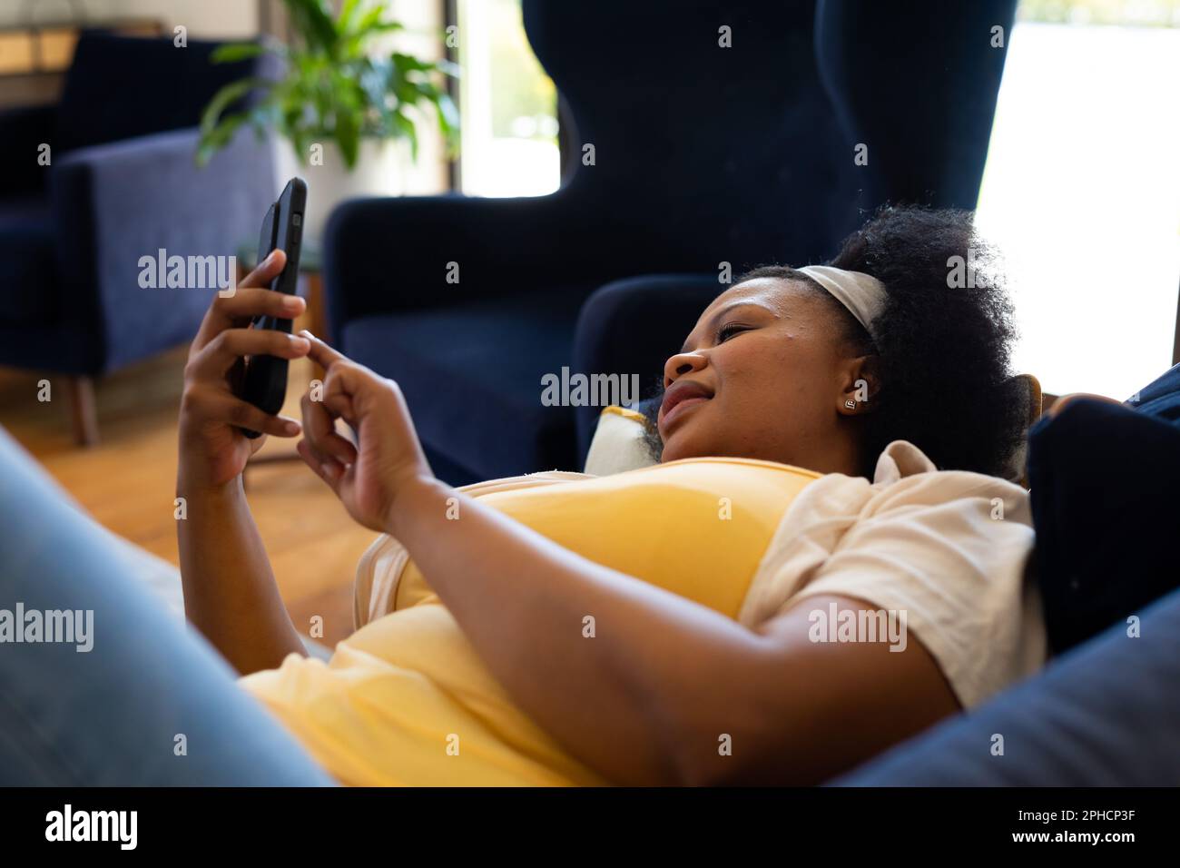 Happy Plus Size African American Woman Lying On Sofa And Using