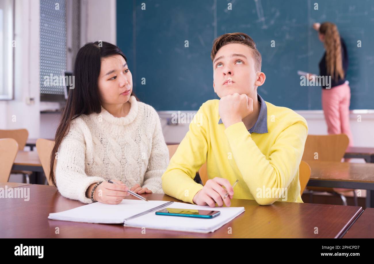 Chinese girl student explaining learning material to bored classmate ...