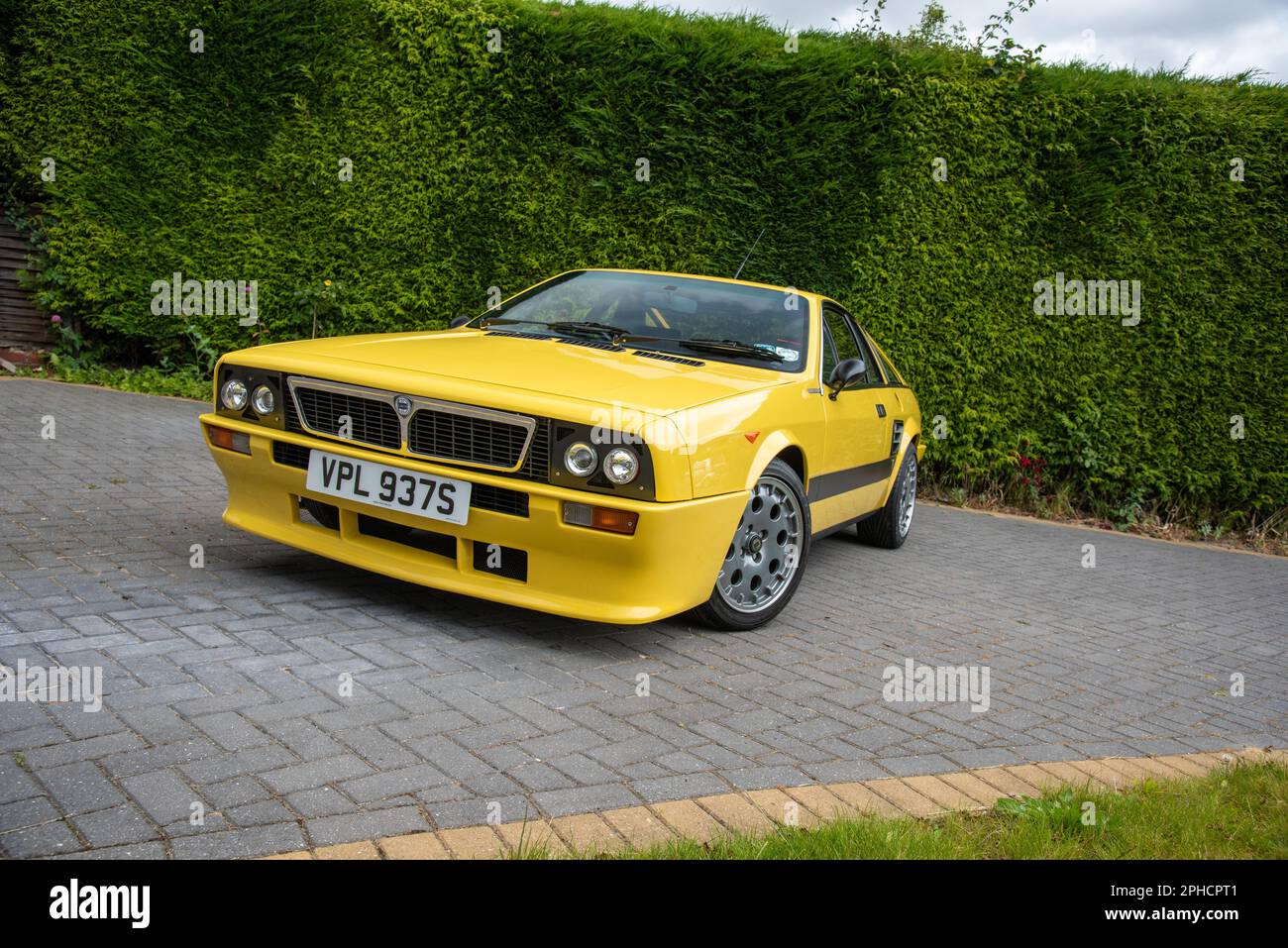 Yellow Lancia Montecarlo parked on a drive with a green hedge behind ...
