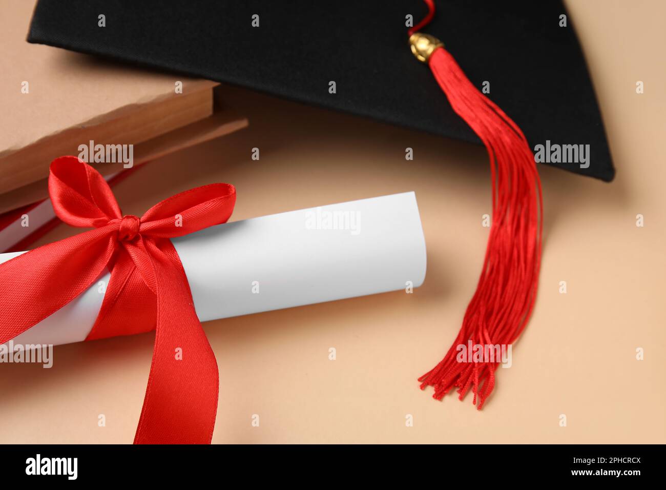 Diploma with red ribbon, graduation hat and books on beige background ...