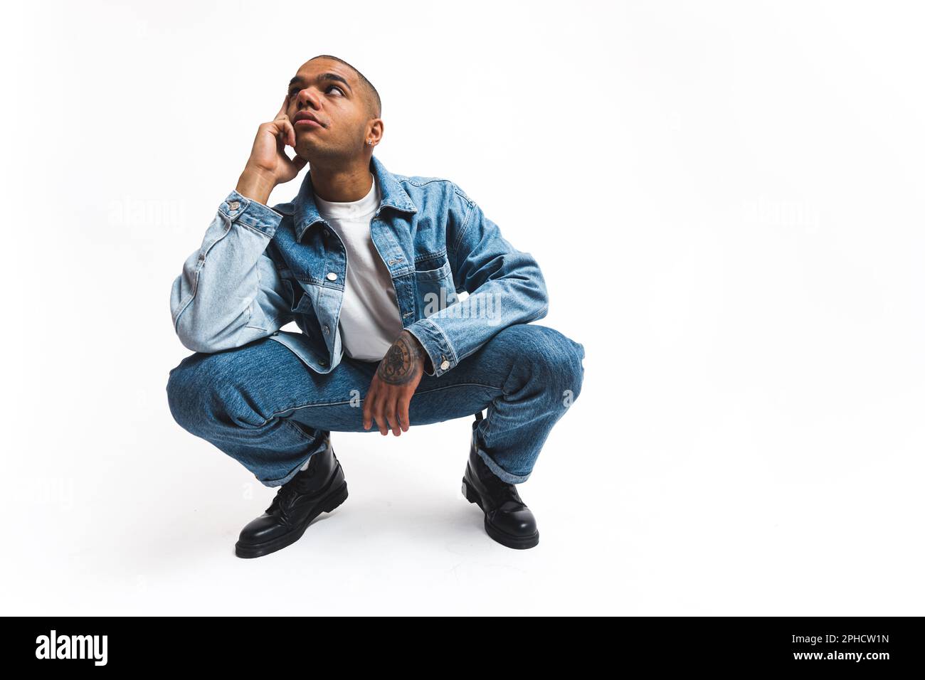 Handsome man in fashionalbe denim suit squatting in white cyclorama ...