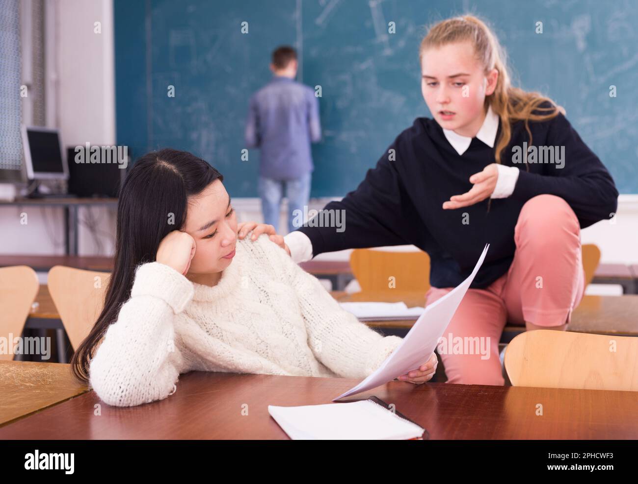 Teen female student supporting upset Chinese girl in classroom Stock ...
