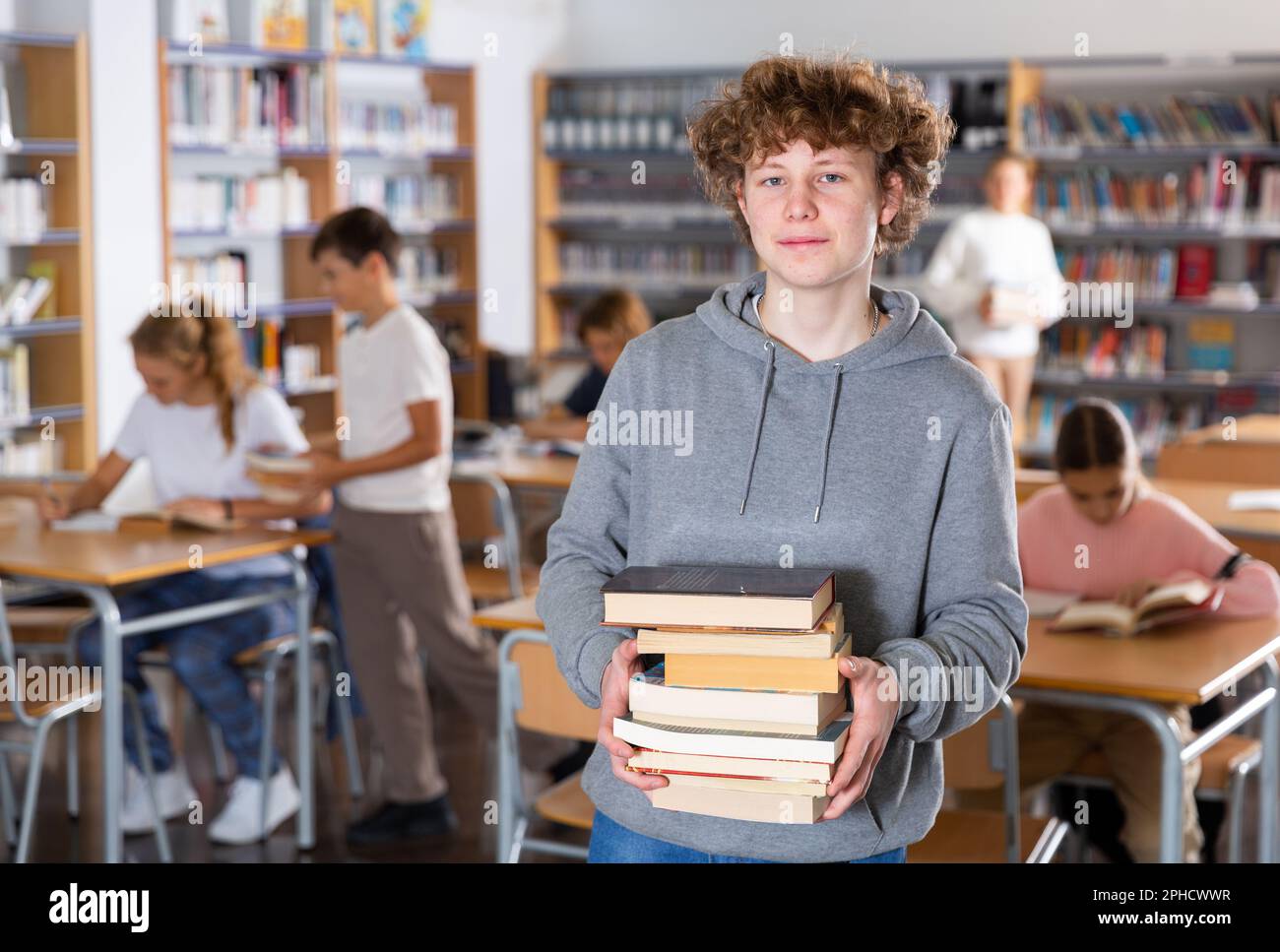 Teenager boy standing with a stack of books in library Stock Photo - Alamy