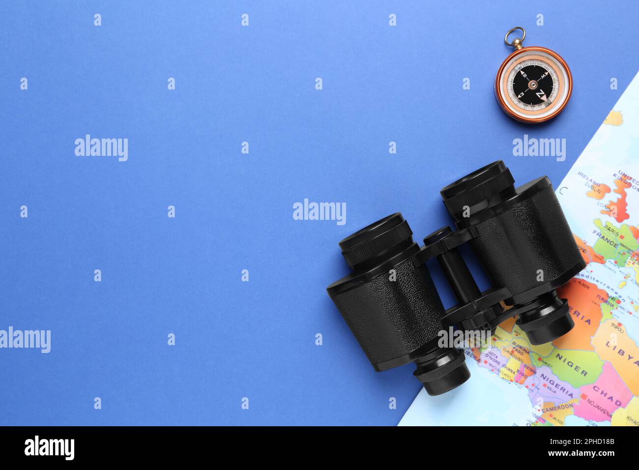 Modern binoculars, compass and world map on blue background, flat lay. space for text Stock ...